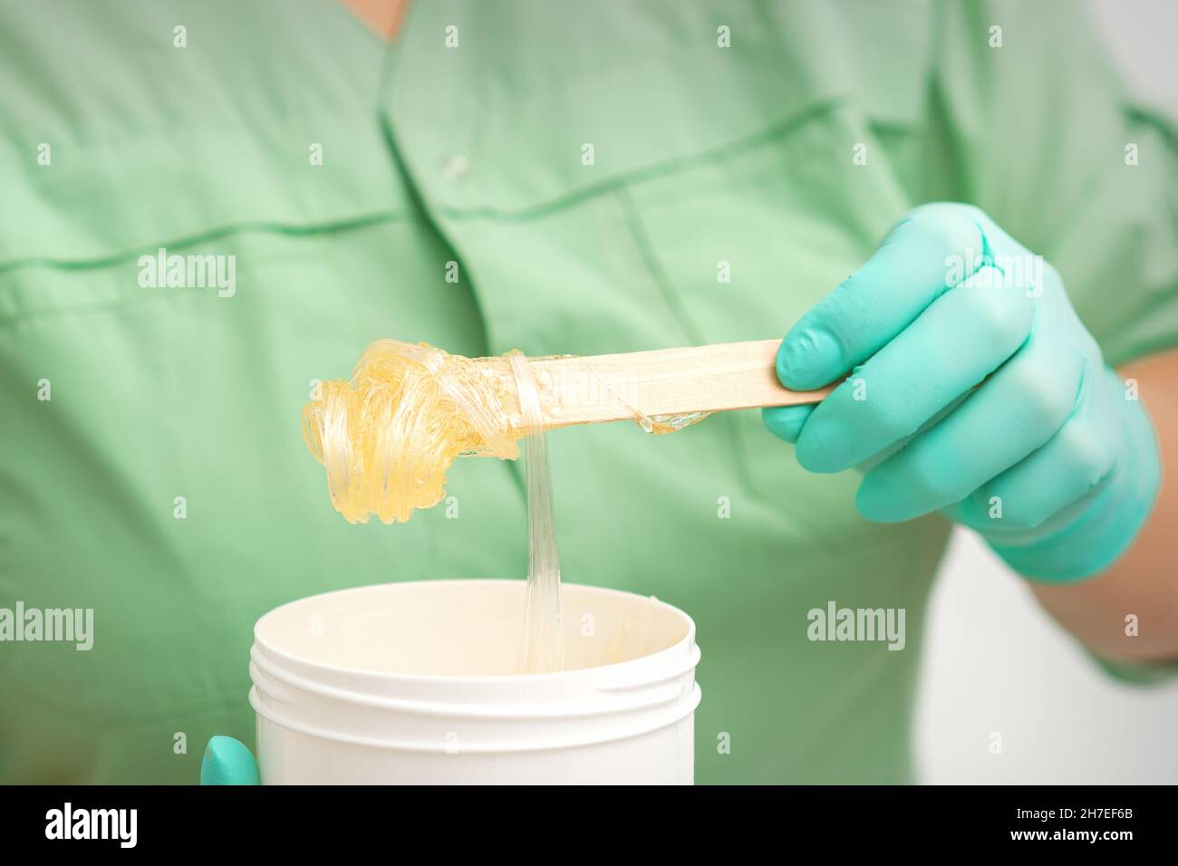 Liquid yellow sugar paste for depilation on a stick flows into the jar ...