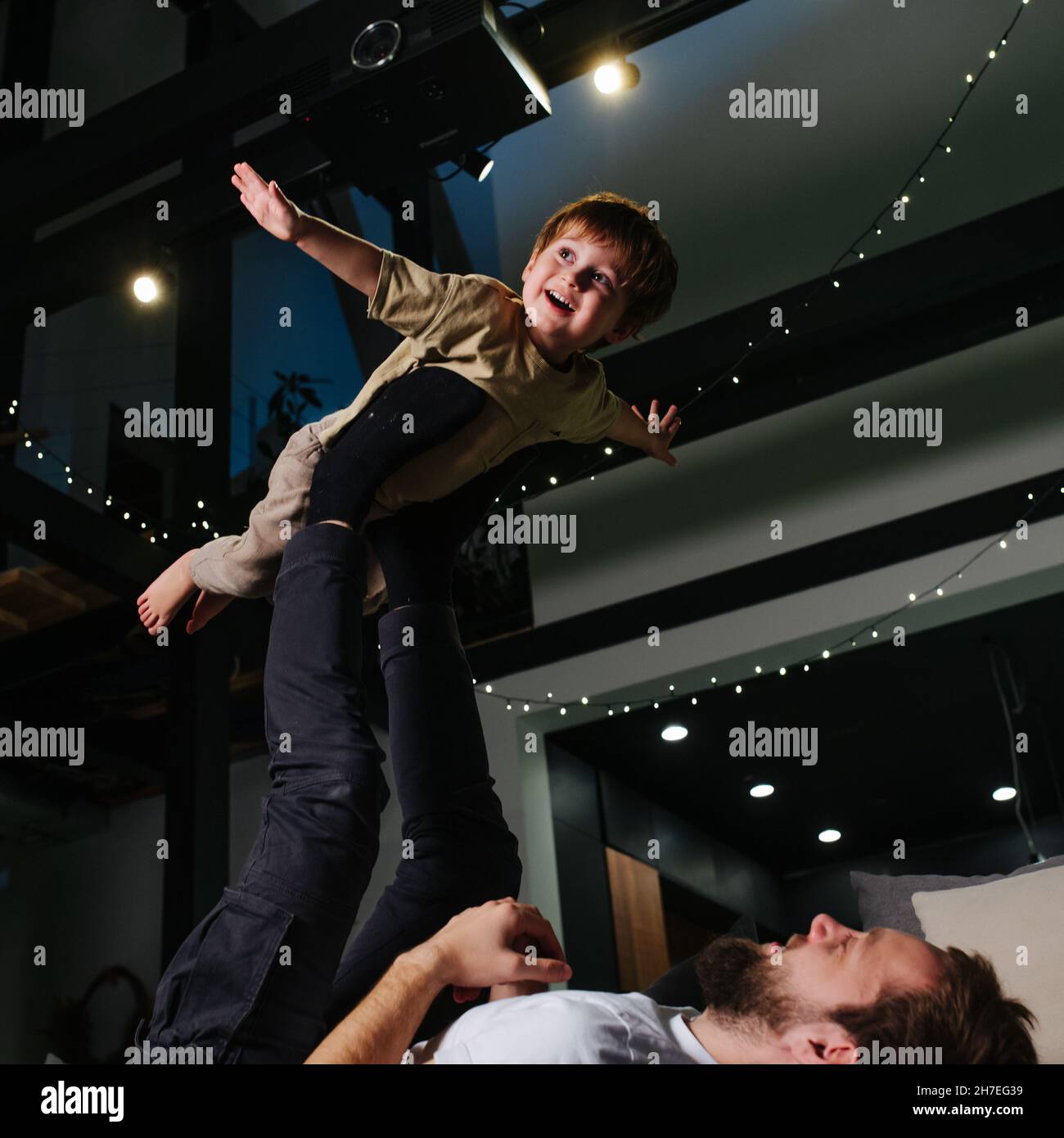 Square image of father lifting his happy child with his legs. He is ...