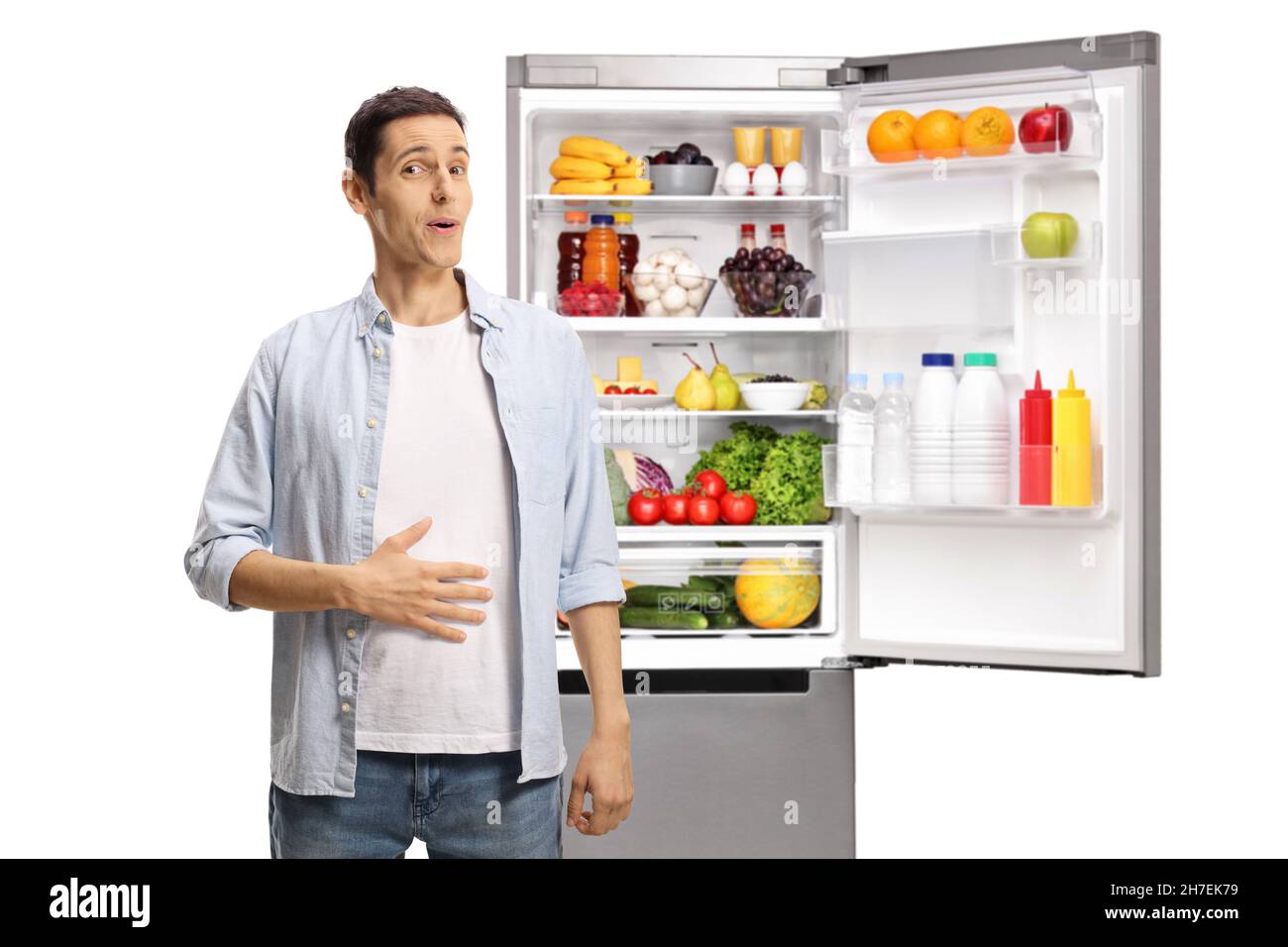 Young man holding his hand on his stomach in front of an open fridge ...