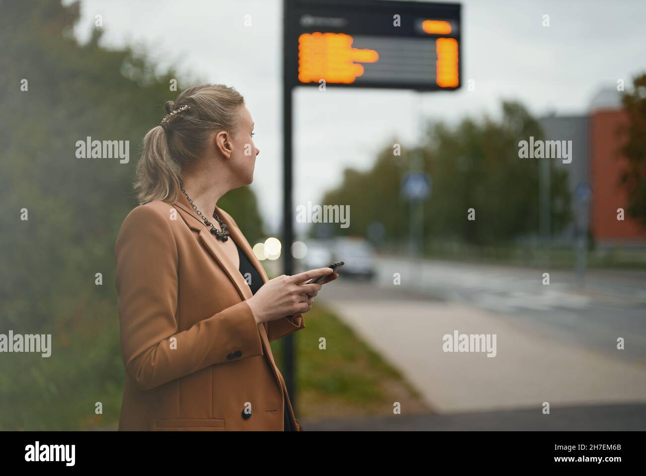Woman with smartphone is waiting for bus at bus stop Stock Photo - Alamy