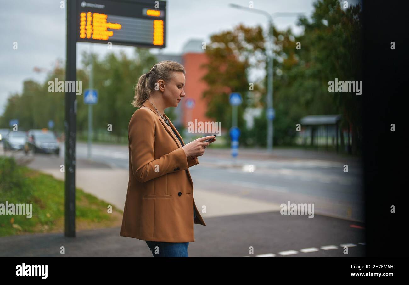Woman with smartphone is waiting for bus at bus stop Stock Photo - Alamy