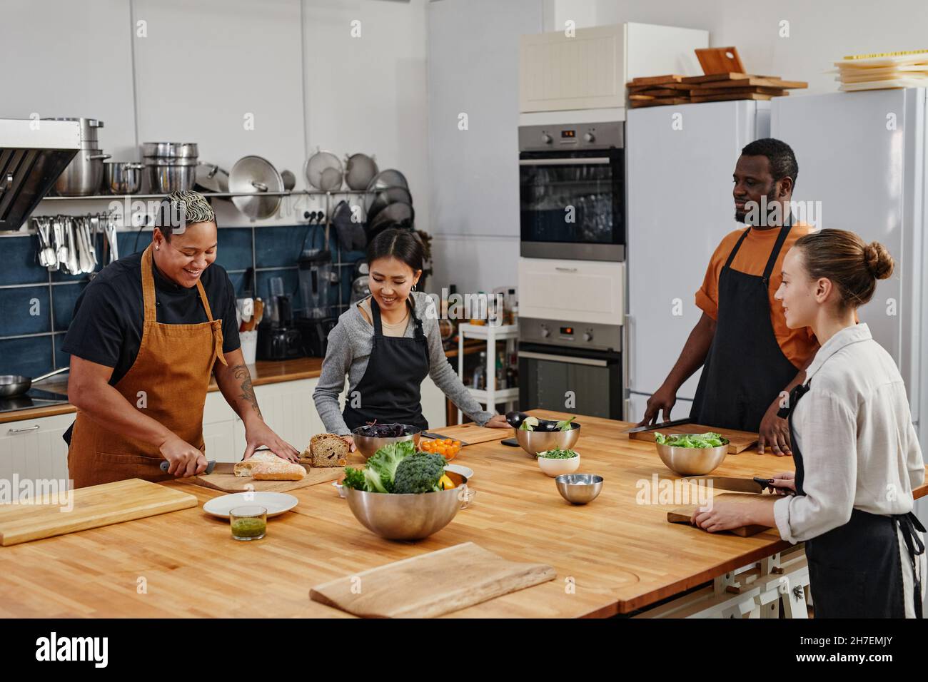 Diverse group of people laughing while cutting vegetables together in ...