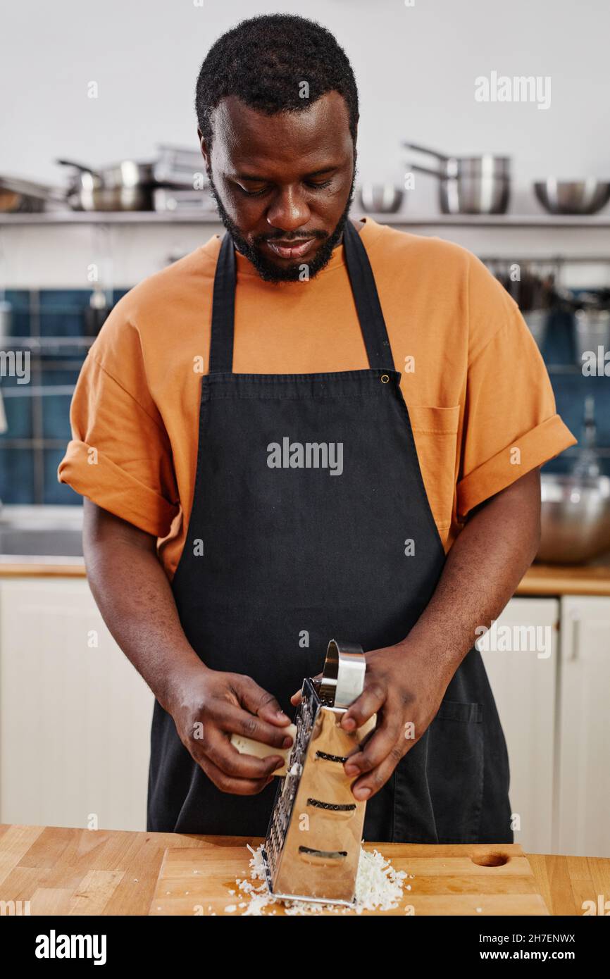 Vertical waist up portrait of African-American man grating cheese while ...