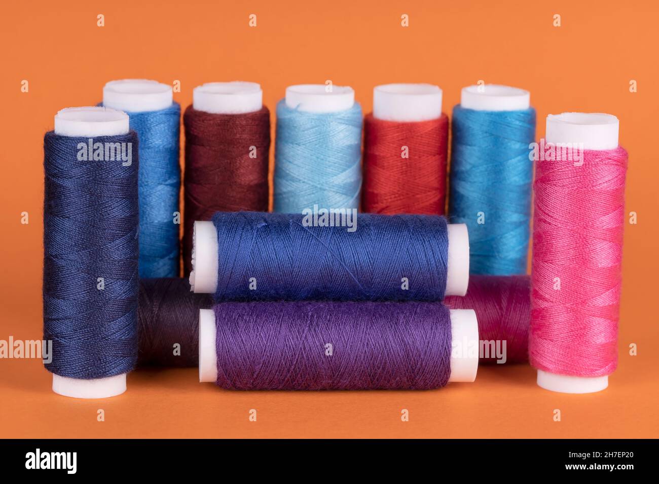 Bobbins of sewing thread of different colors isolated on orange ...