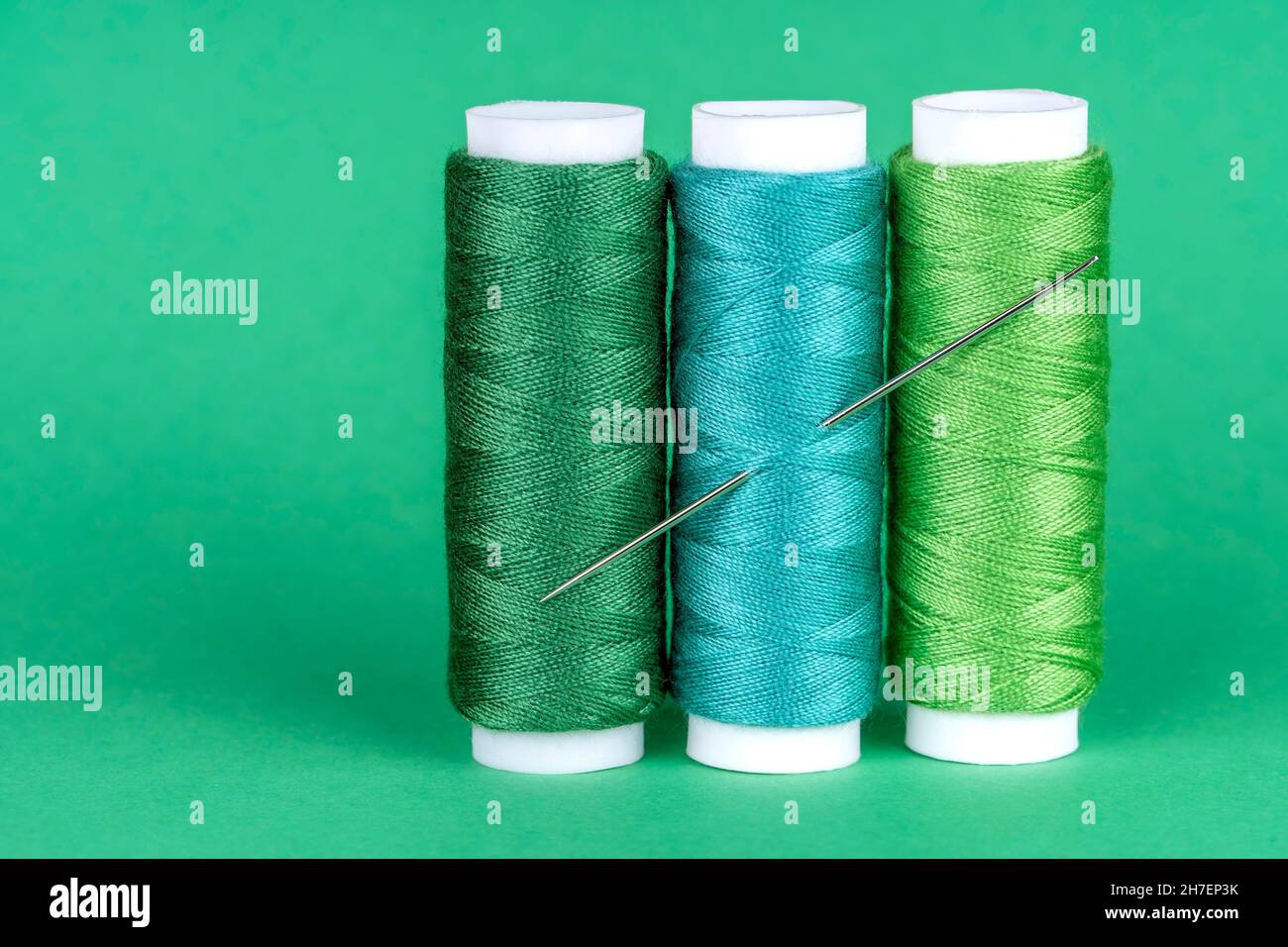 Three spools of sewing thread of different shades of green with a ...