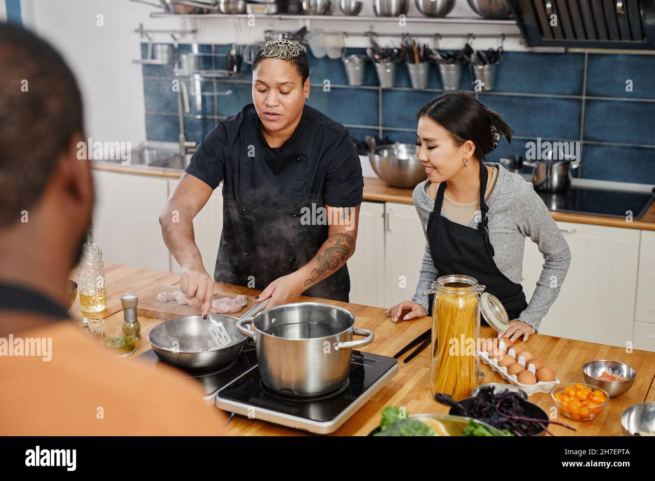 Portrait of tattooed female chef frying meat during cooking class in ...