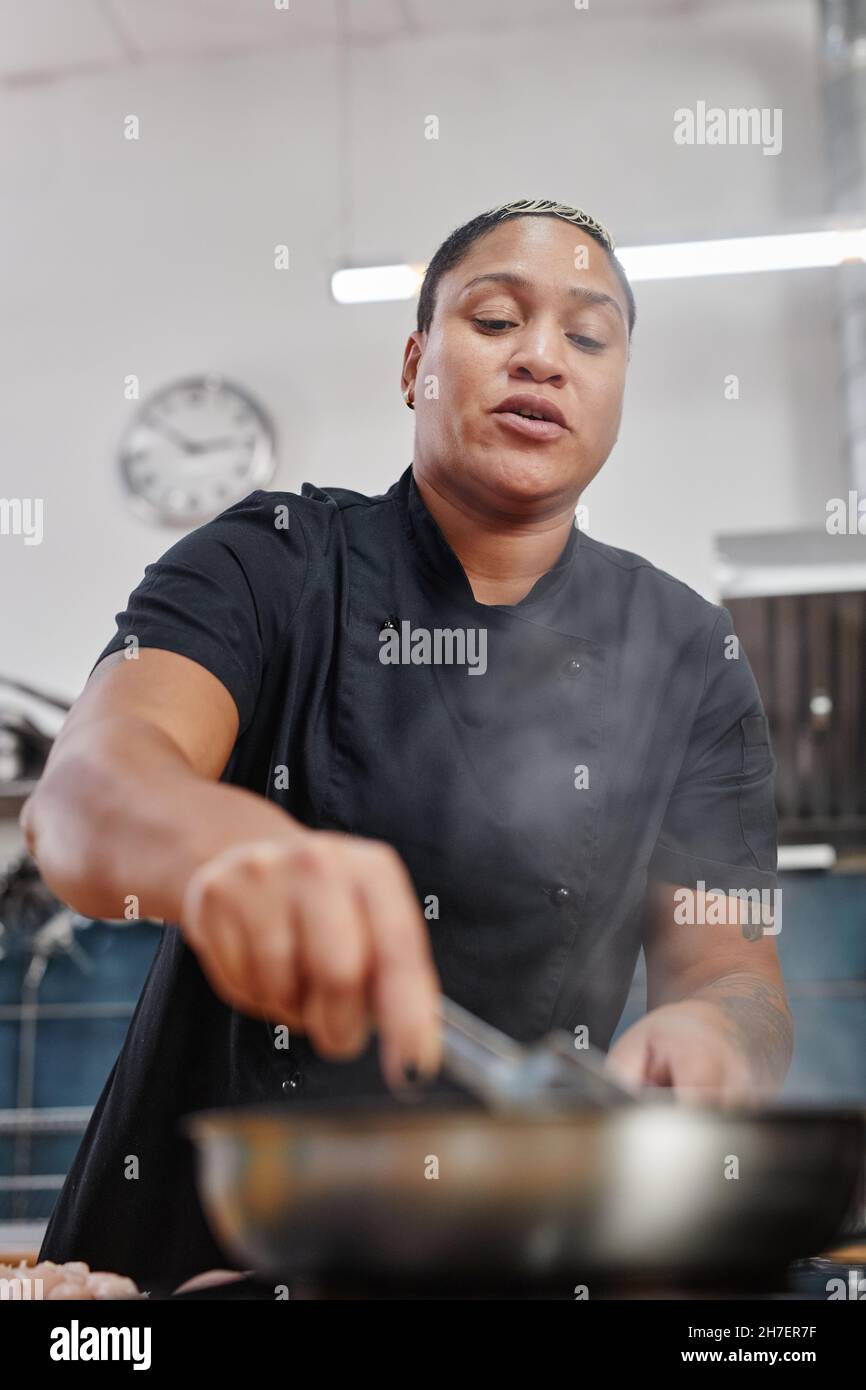 Low angle portrait of Latin-American female chef frying meat while ...