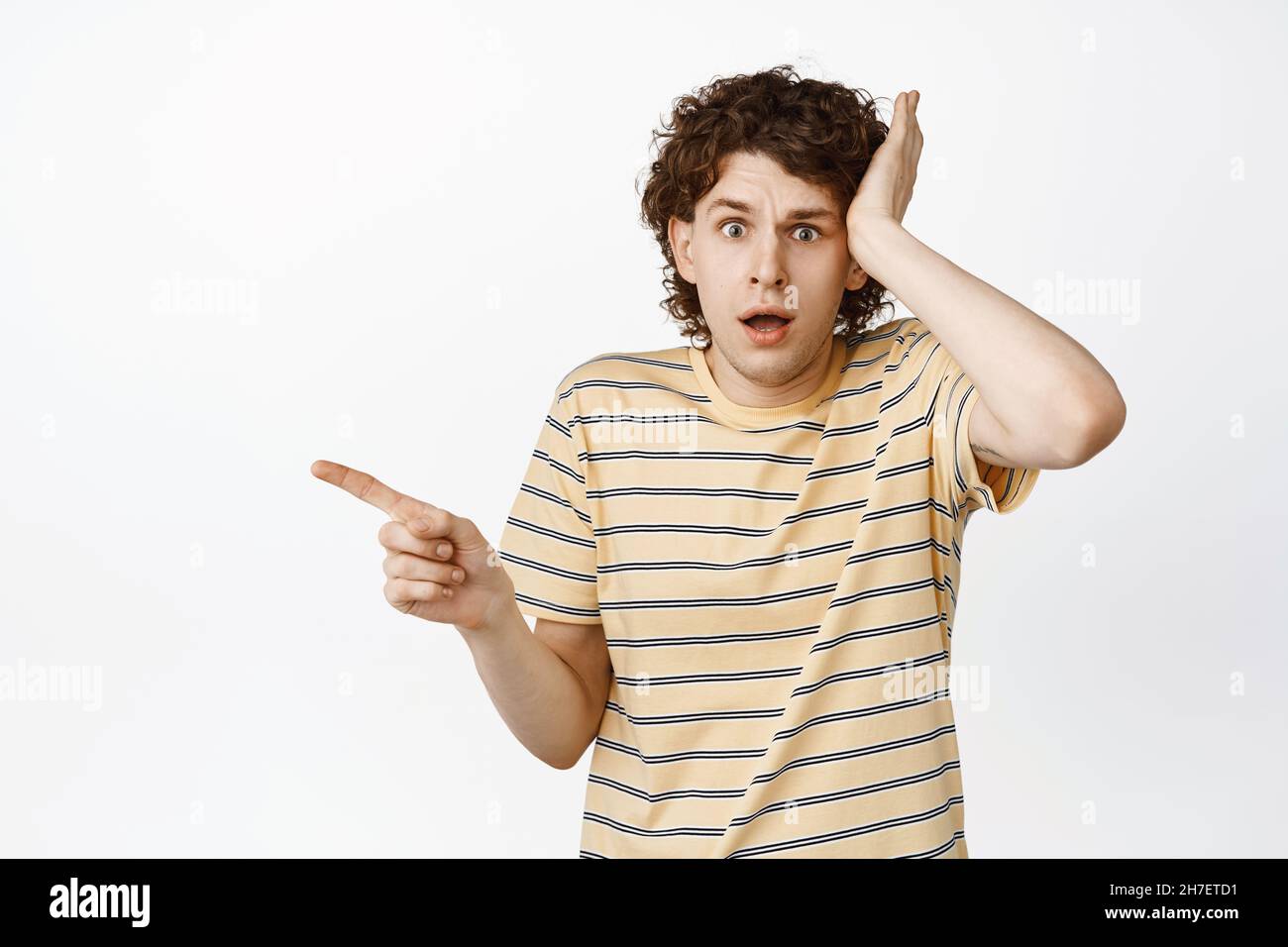 Shocked and anxious young man, pointing finger left, hold hand with ...