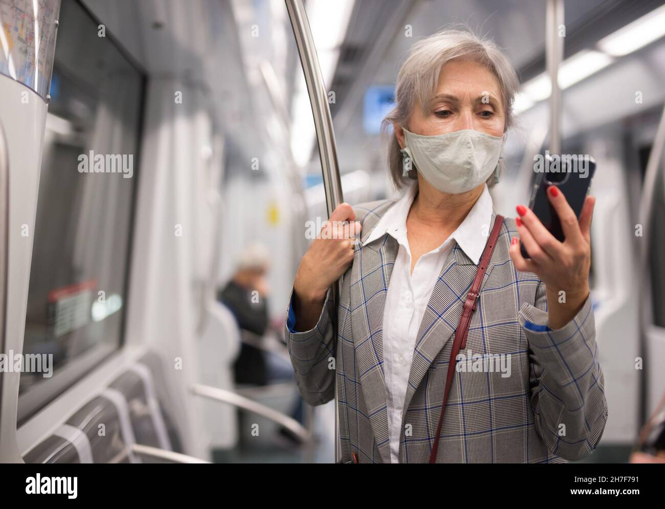 Senior lady in mask standing in metro train and using smartphone Stock ...