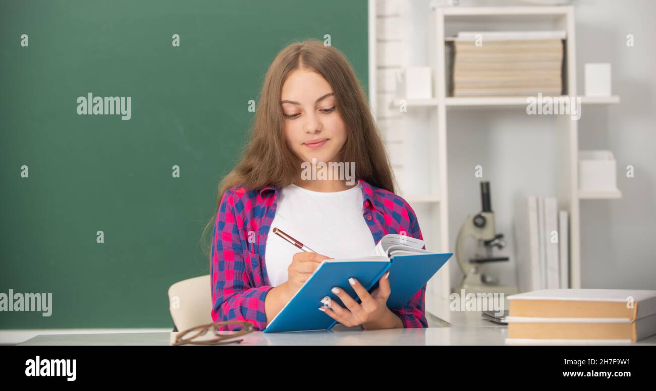 kid making notes in copybook in classroom at blackboard, erudition ...