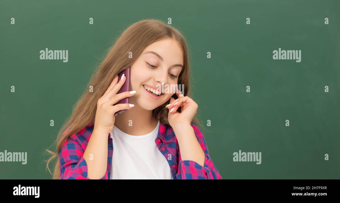 happy kid speaking on smartphone in classroom at blackboard, copy space ...