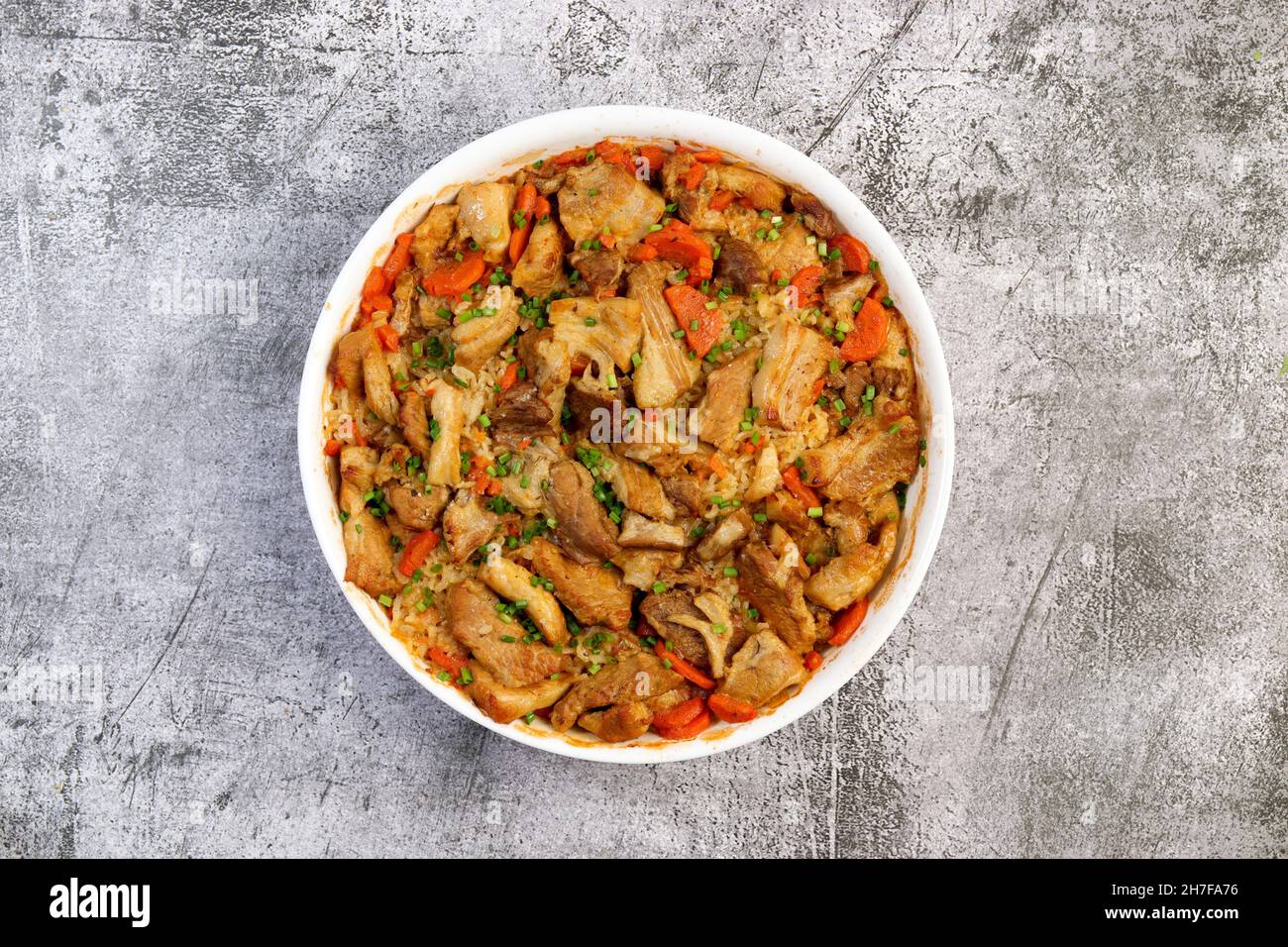 Oven baked pork belly with rice and vegetables in a white baking dish ...