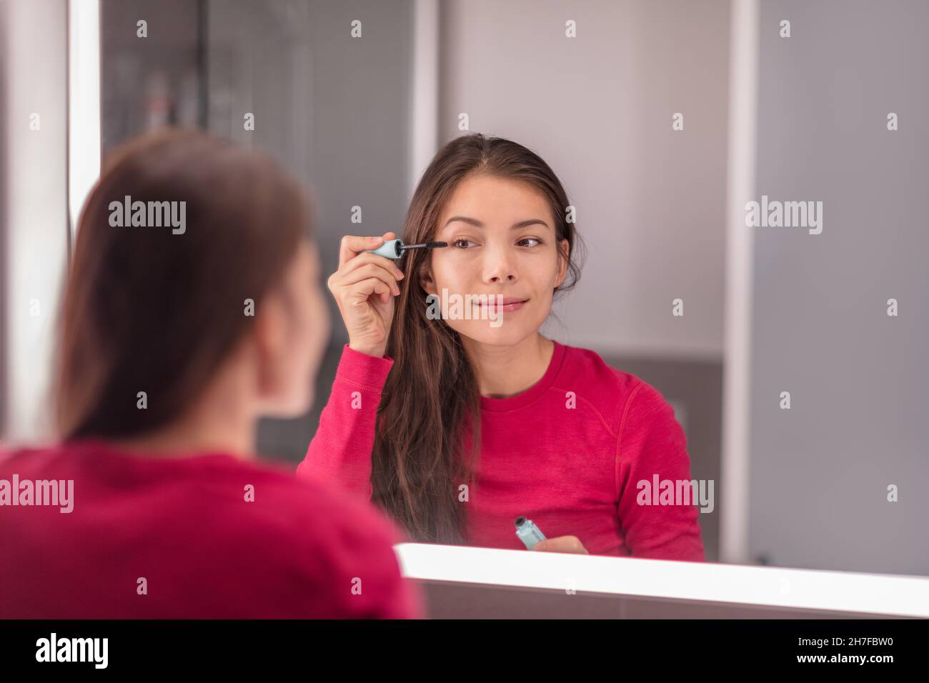 Woman putting make-up in the LED lighted mirror getting ready morning ...