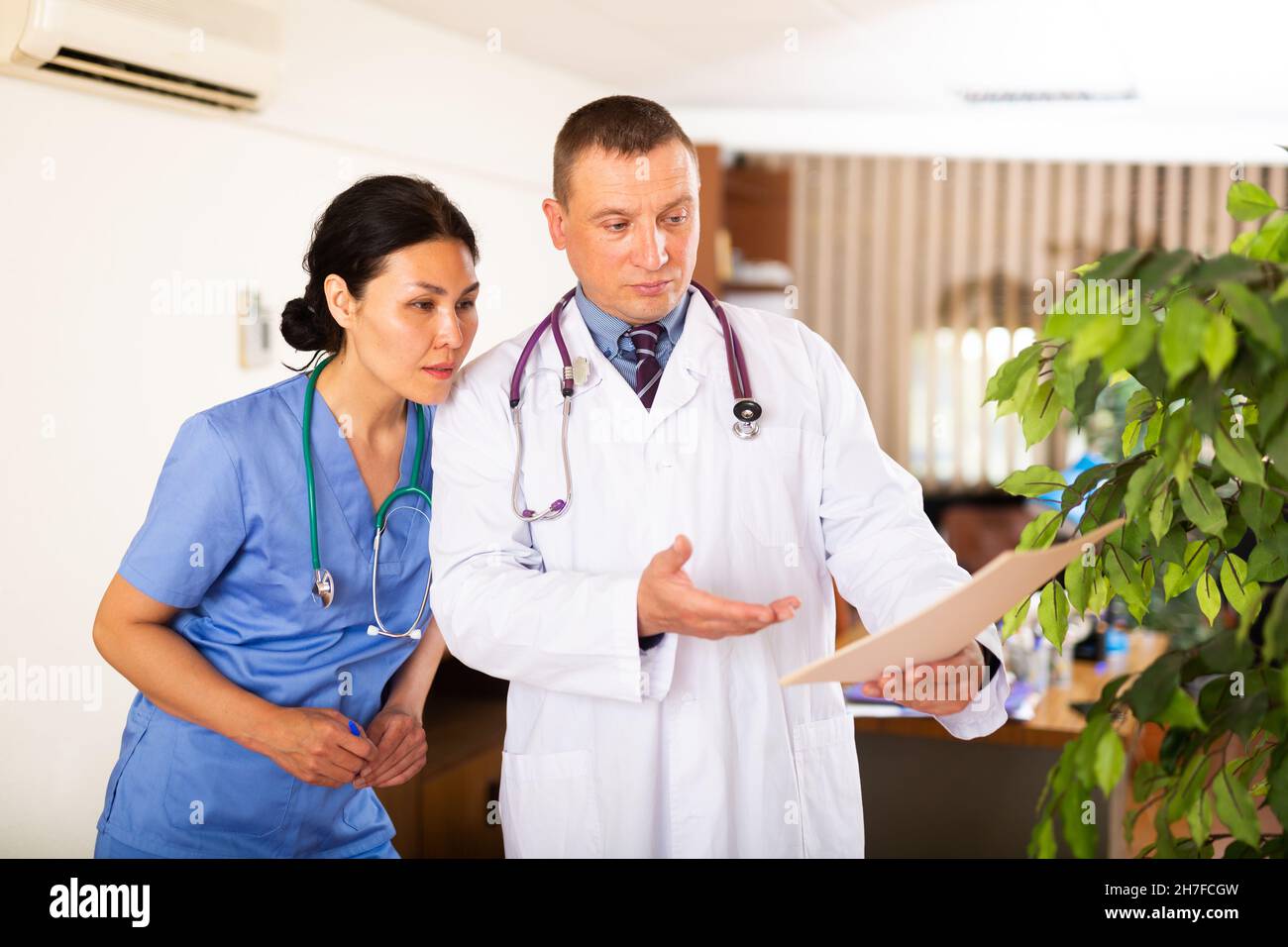 Two doctors discussing medical card of patient in office Stock Photo ...