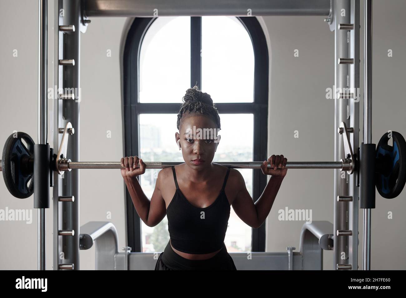 Serious slim Black sportswoman getting ready to lift heavy barbell when ...