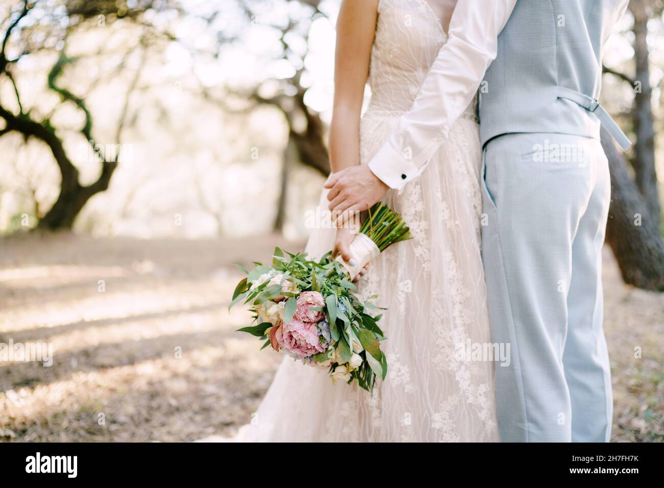 The bride and groom are embracing among the trees, the bride holds ...