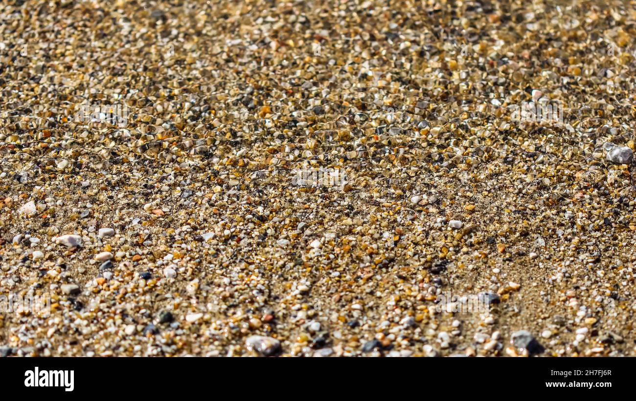 A background of sand, small pebbles and flowing waves on the sea beach ...