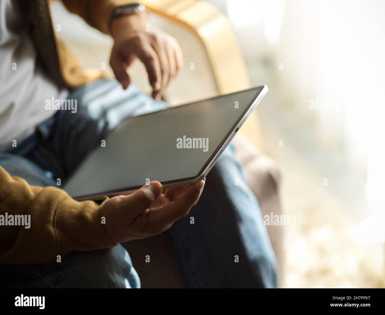 An adult man sitting at his arm chair and using modern digital tablet ...