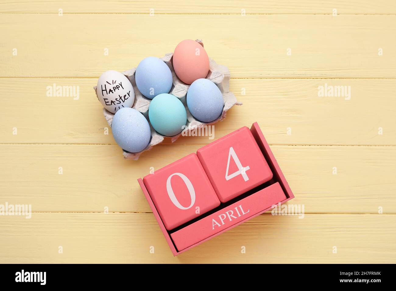 Calendar with date April 4 and painted eggs on color wooden background ...