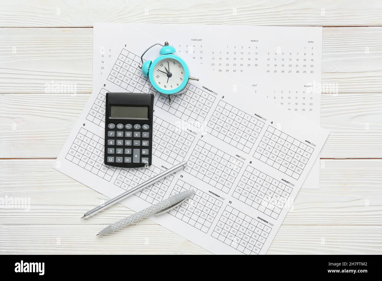 Paper calendars with stationery and alarm clock on white wooden ...
