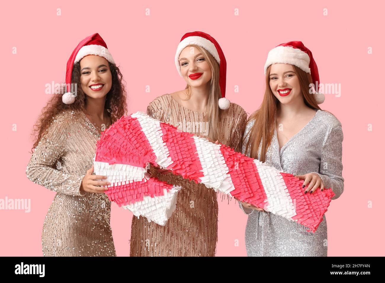 Beautiful young women in Santa hats and with candy cane pinata on color ...