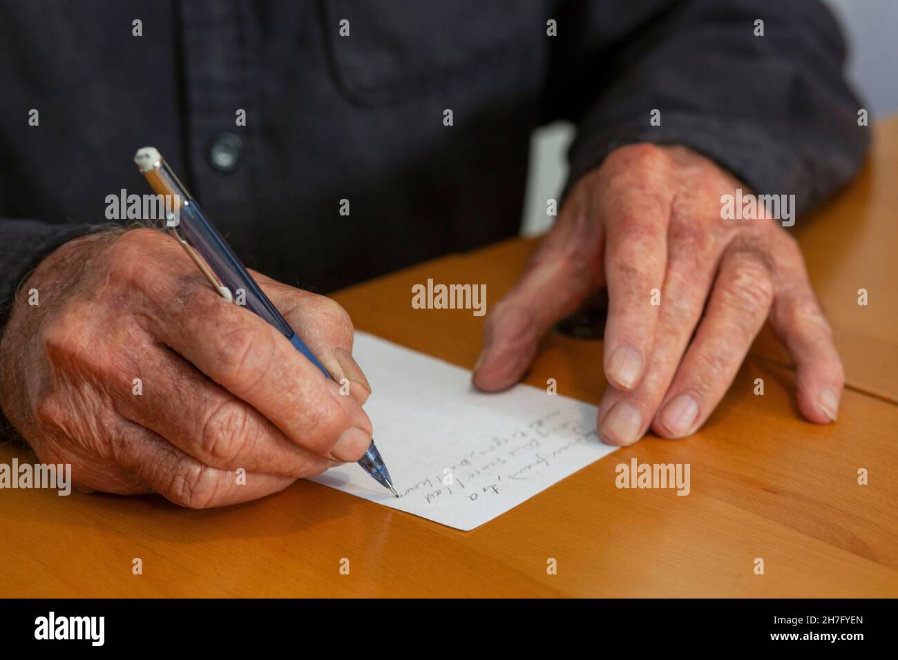 A close up of the hands of an elderly man's hands writing a note MR ...