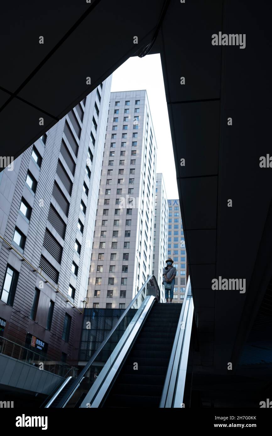 person standing on the top of escalator, surrounded by high buildings ...