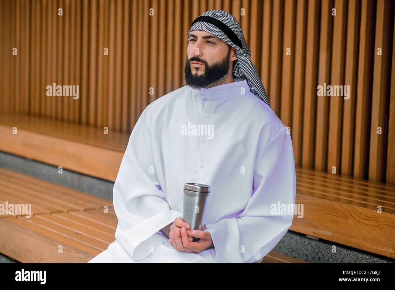 Young arabian man sitting on a wooden bench with metal cup Stock Photo ...