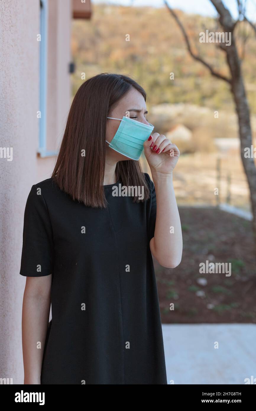Vertical shot of a Caucasian female coughing while wearing a face mask ...