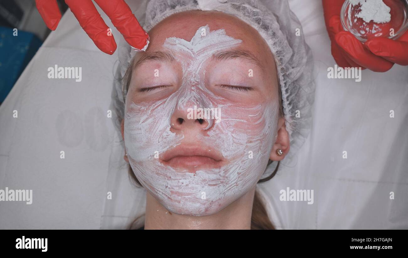 Application of a cream mask on the face of a girl with problem skin in ...