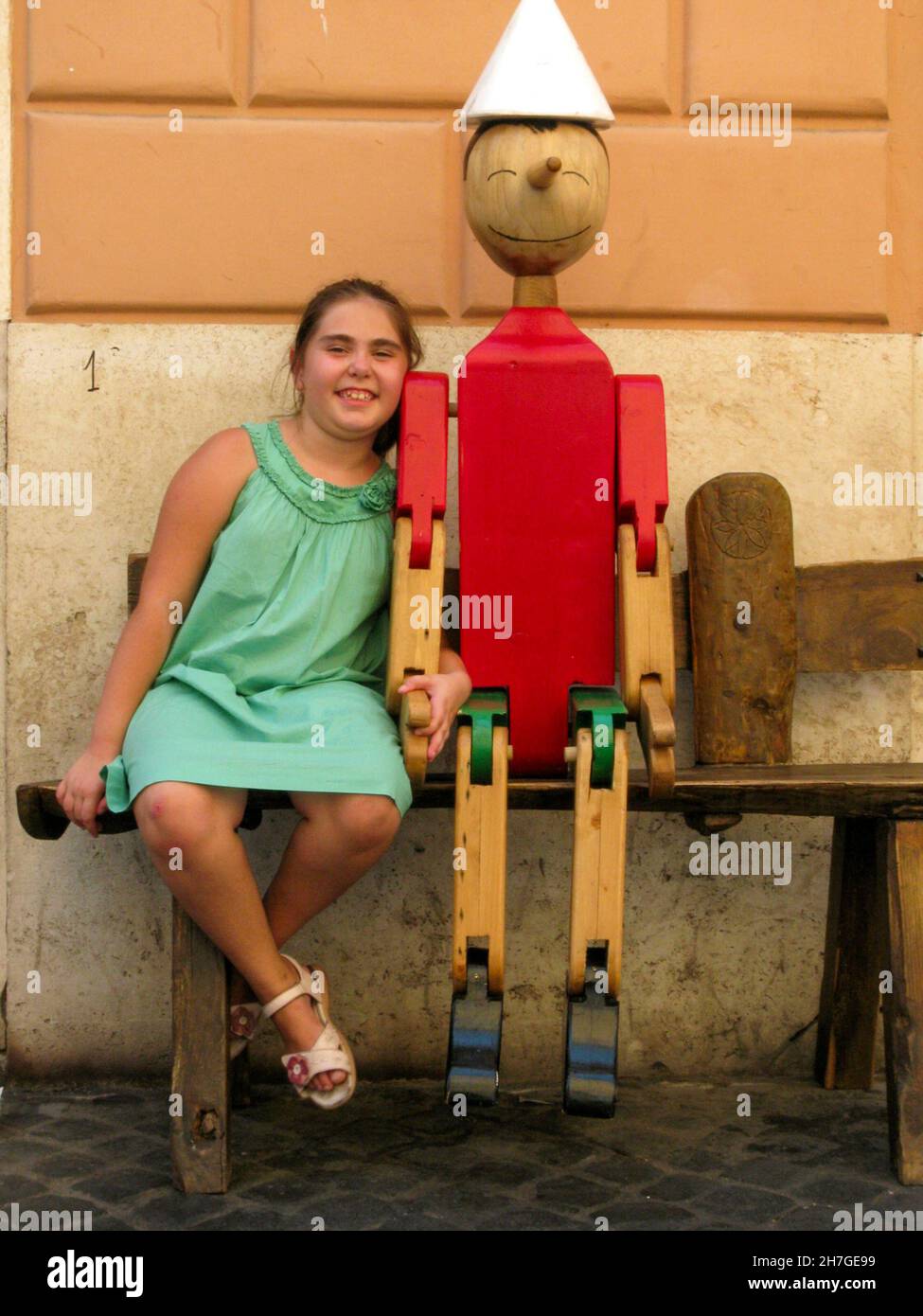 Young girl tourist posing for photo sitting on bench with Pinocchio ...