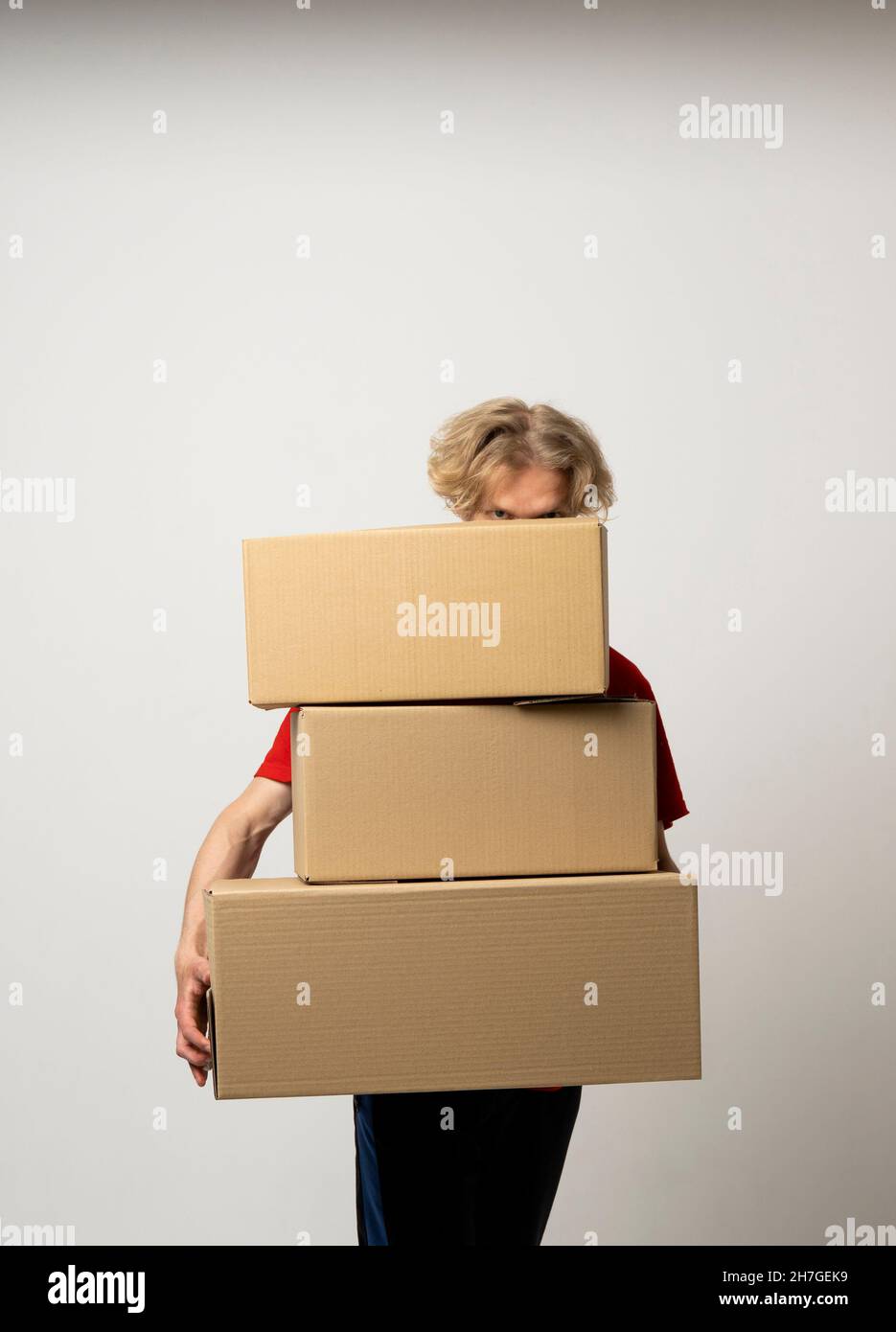 Delivery man in a red uniform holding a stack of cardboard boxes ...