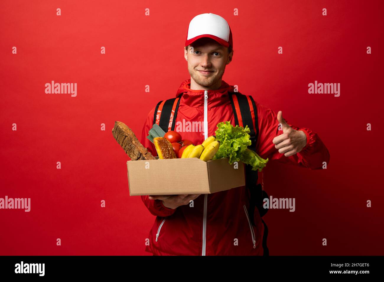 Grocery delivery courier in red uniform with a paper box with food ...