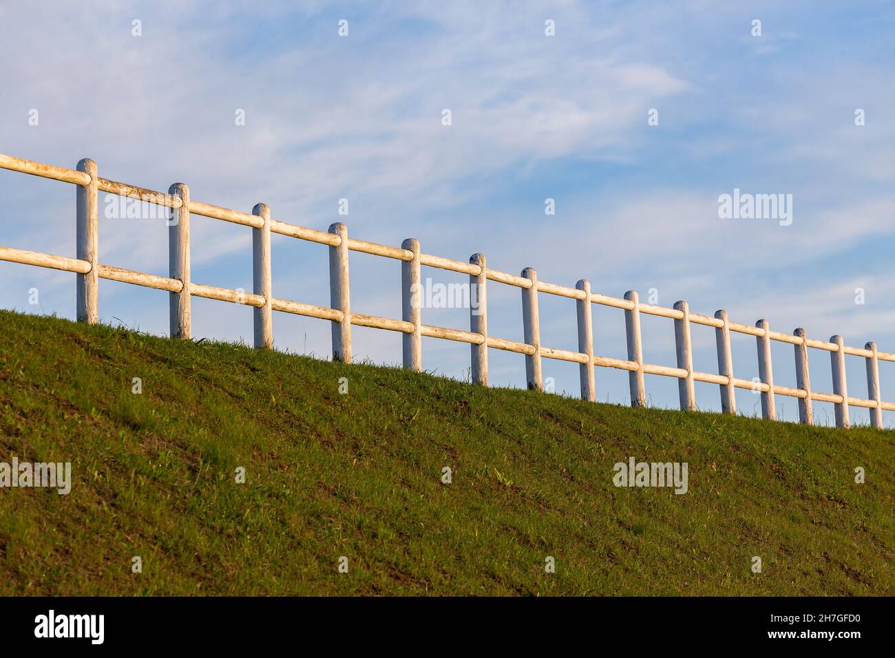 White wood round pole fence across the grass embankment against morning ...