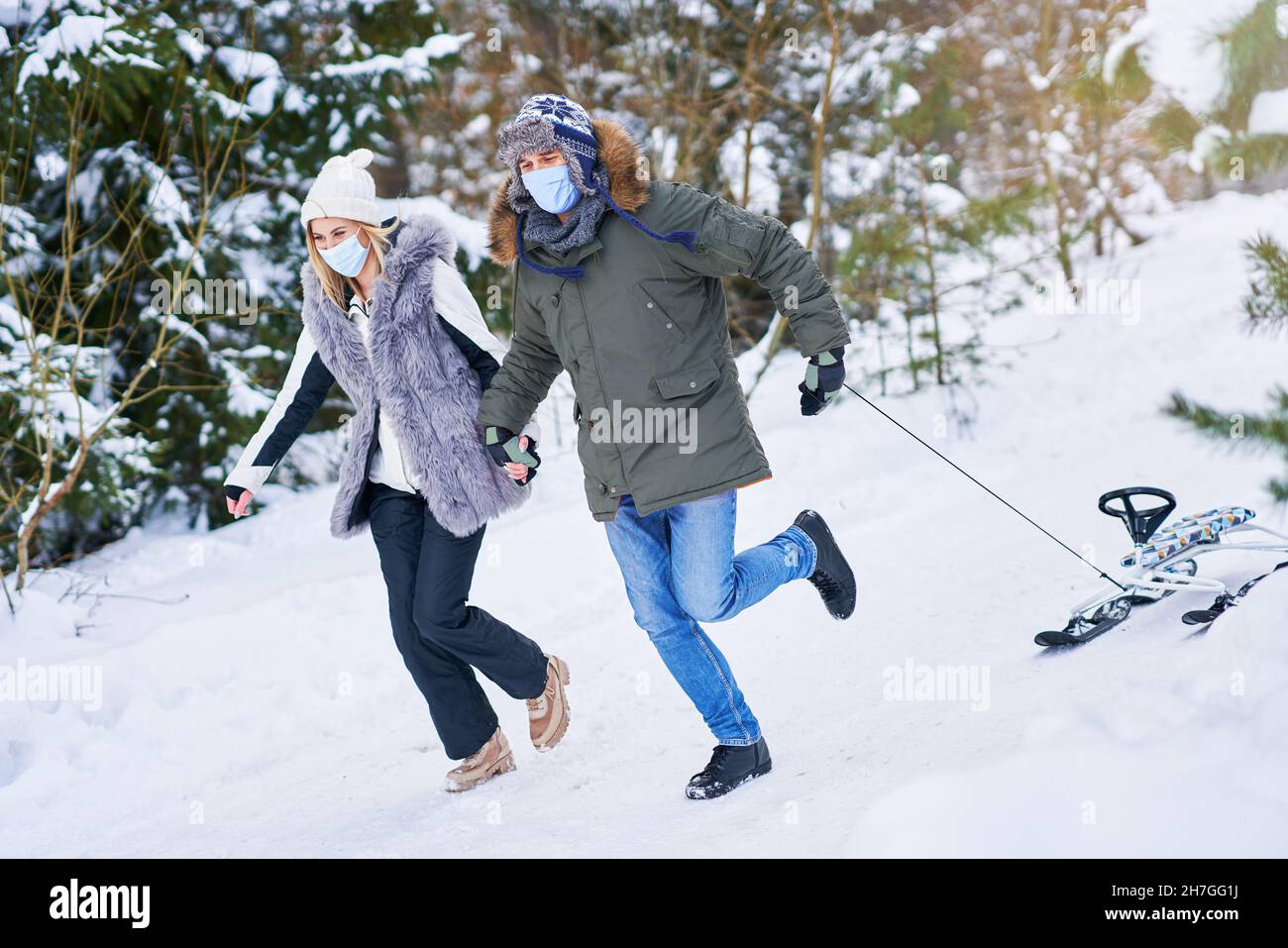 Couple having fun with sledge on snow wearing mask Stock Photo - Alamy