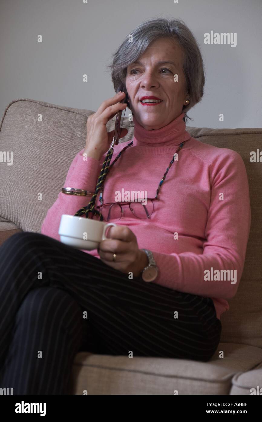 Happy Mature Woman Talking Cell Phone While Sitting On Sofa Having