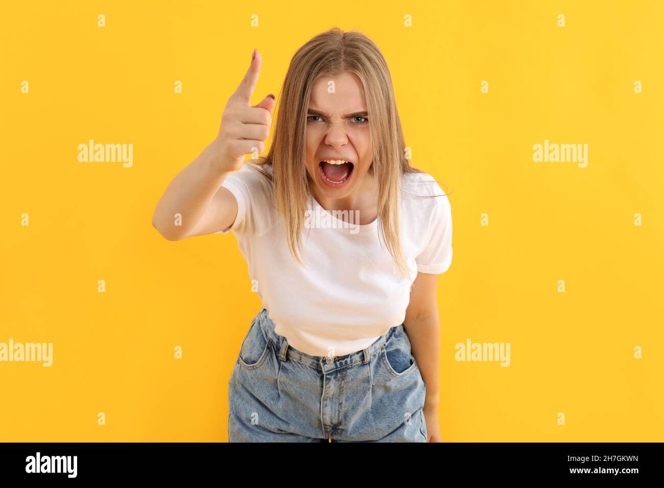 Young angry girl in jeans on yellow background Stock Photo - Alamy
