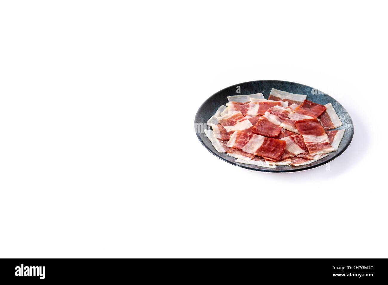 Spanish serrano ham slice on black plate isolated on white background ...