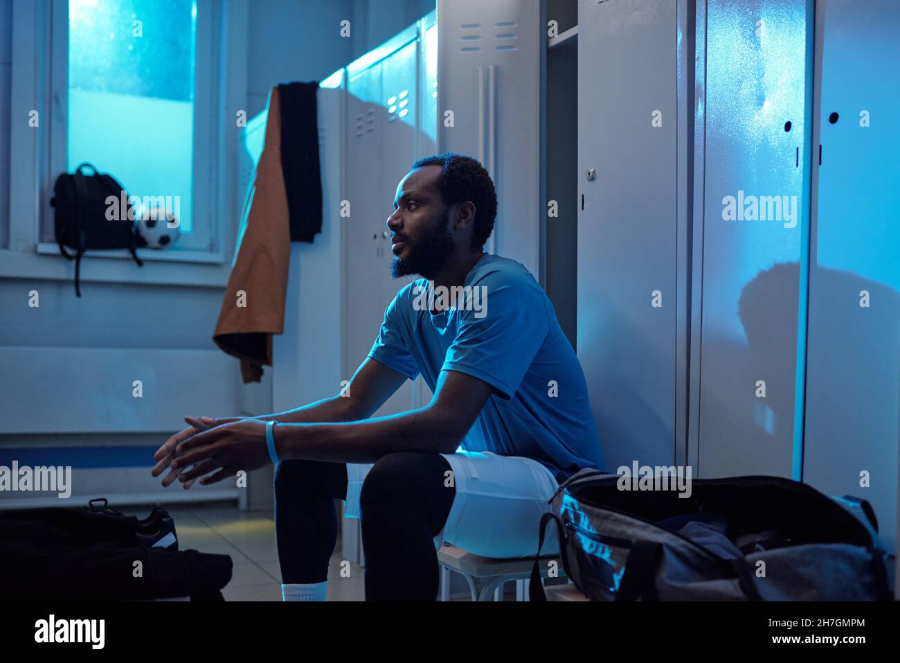 Young restful professional soccer player in sports uniform sitting ...