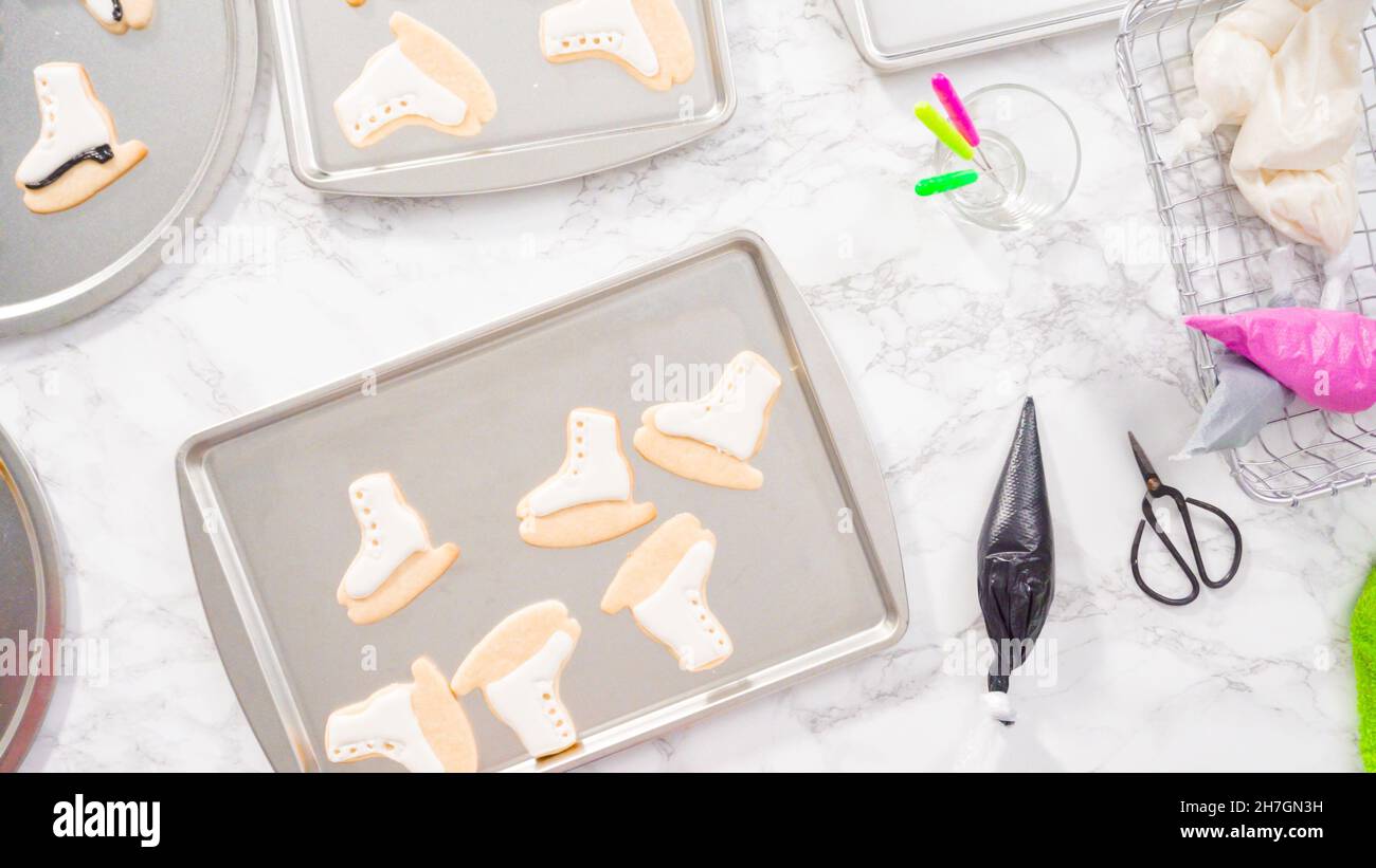 Flat lay. Decorating ice skate shaped sugar cookies with black color ...