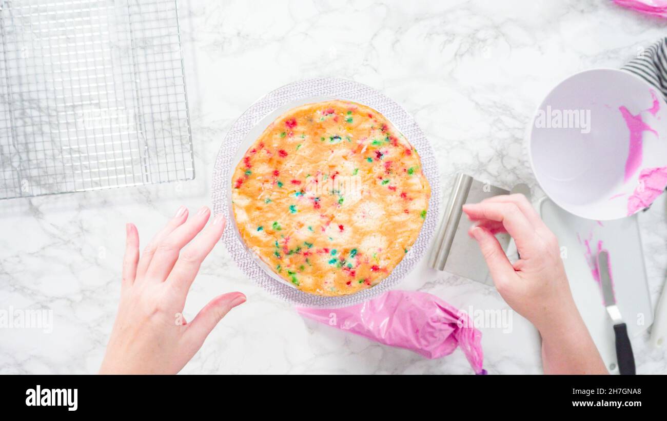 Flat lay. Step by step. Frosting round funfetti cake layers with pink ...