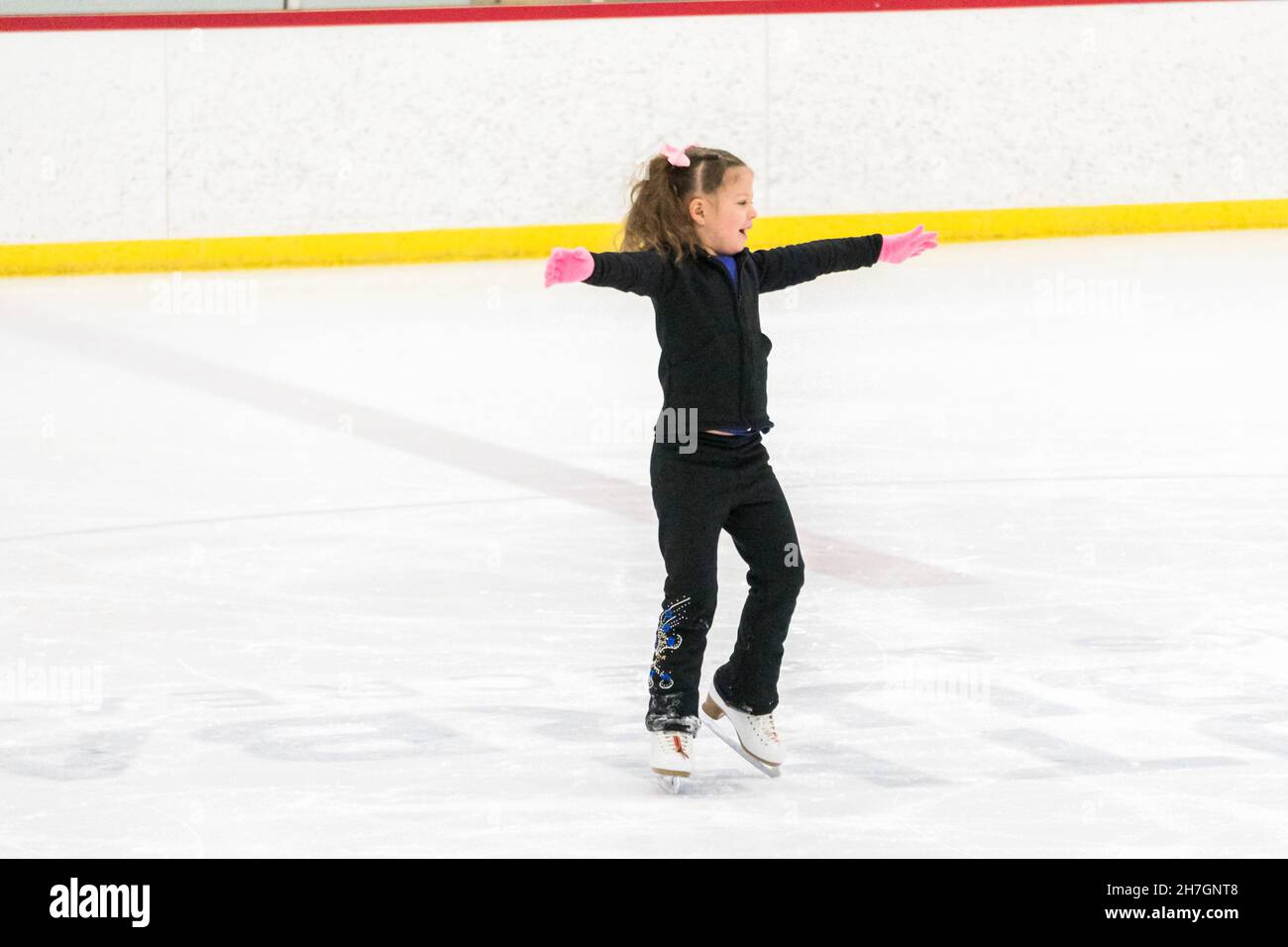 Little girl practicing figure skating moves on the indoor ice rink ...