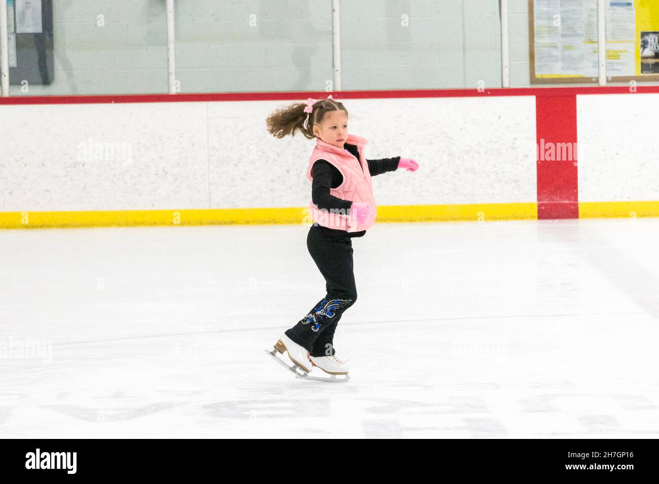 Little girl practicing figure skating moves on the indoor ice rink ...