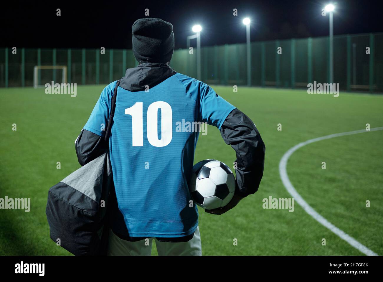 Back of football player with soccer ball and bag moving towards field ...