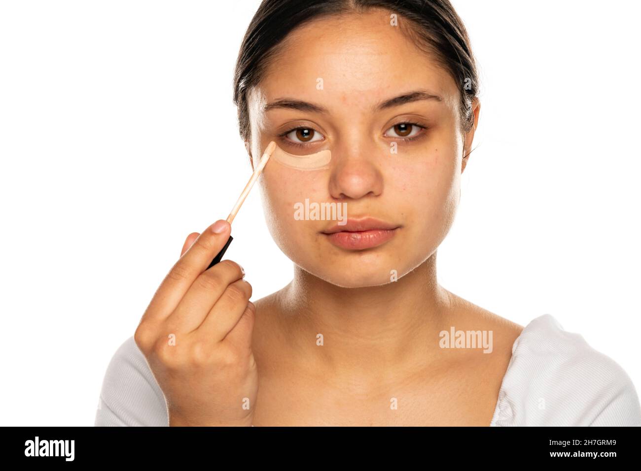 closeup of a young beautiful woman applies concealer under her eye on a ...