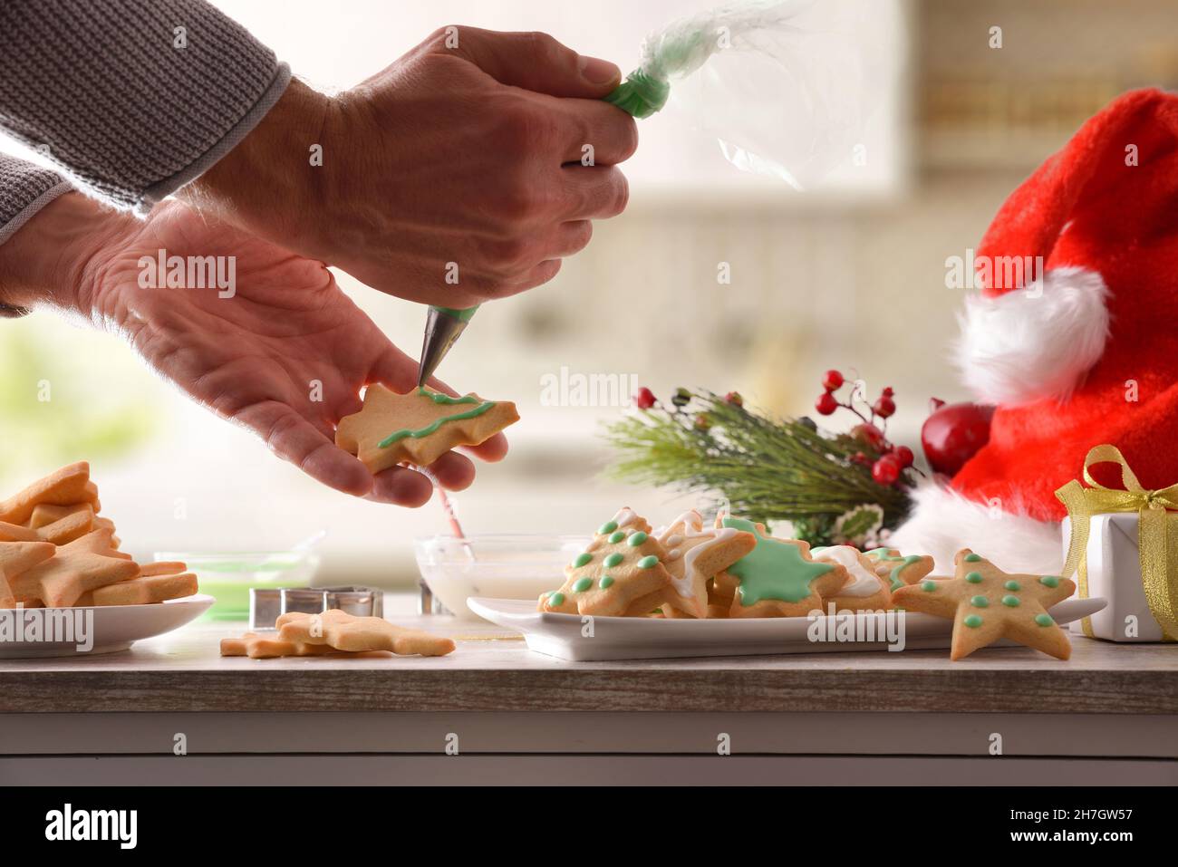 Decorating Christmas-themed cookies with colored icing on kitchen table ...