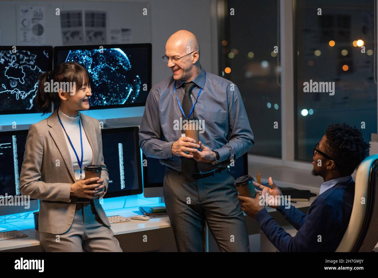 Three happy colleagues with drinks having discussion while sitting by ...
