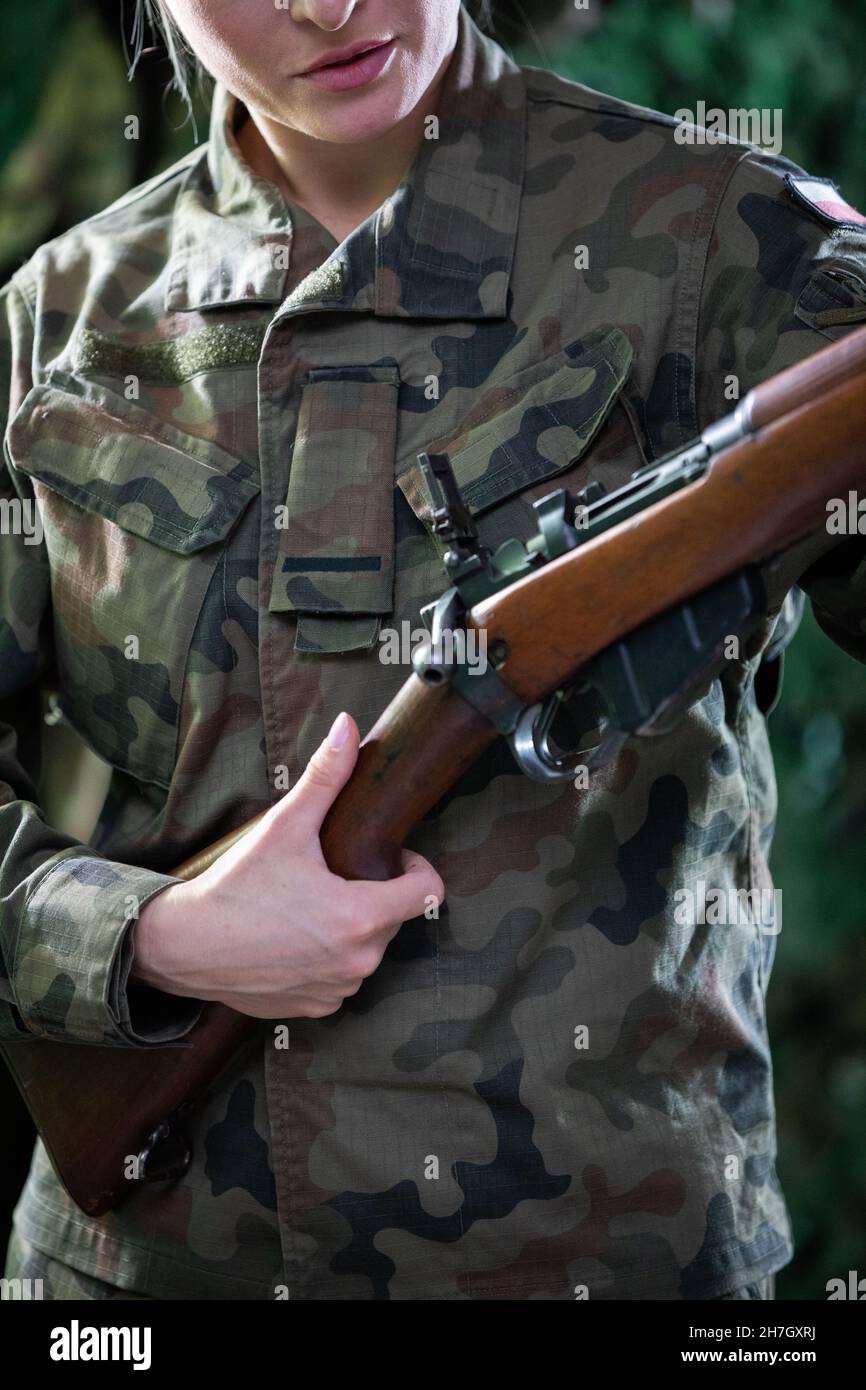 The lady soldier holds a loaded rifle up to the ceiling right in front ...