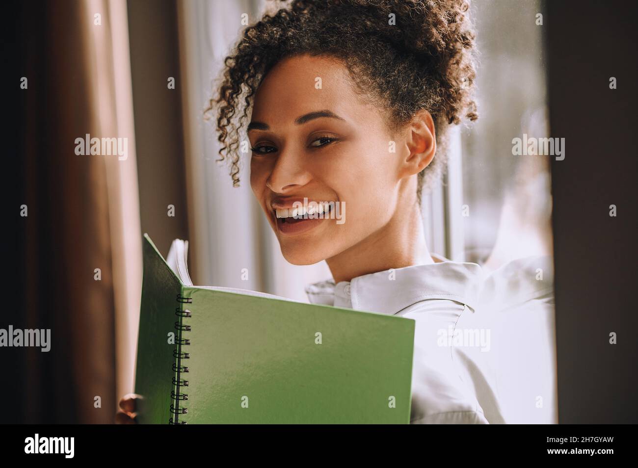 Cute young mulatta holding a notebook and smiling Stock Photo - Alamy