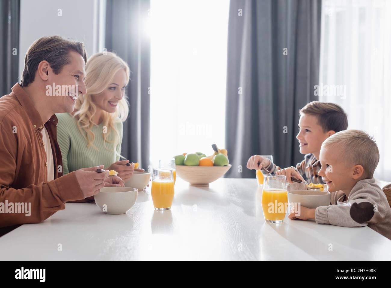 happy parents and sons talking while eating tasty corn flakes for ...